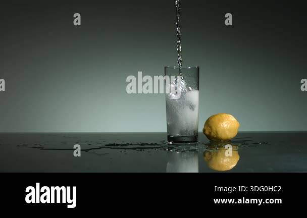 Clear water is poured into a tall glass filled with ice cubes. A whole ...