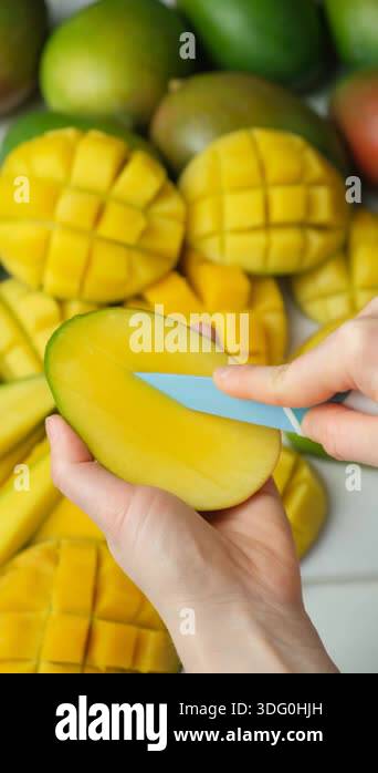 Hands slicing fresh mango with a knife into cubes for hedgehog cut ...