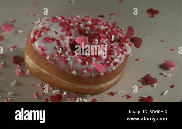 A single donut with white icing and red and pink sprinkles sits on a ...