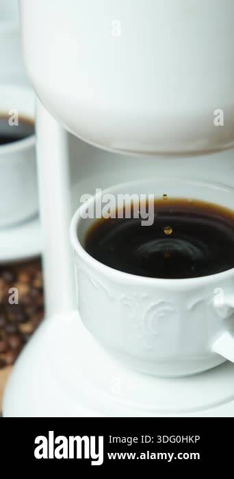 Close-up of fresh hot coffee dripping from a white machine into a cup ...