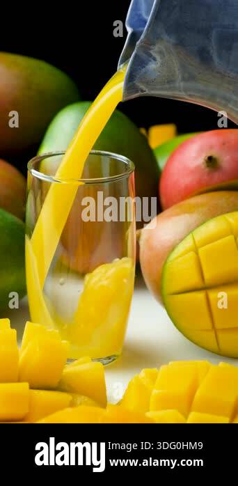 Freshly squeezed mango juice pouring from a jug into a glass, vertical ...
