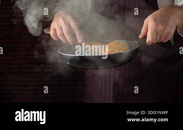 A chef is cooking in a kitchen. He stirs food in a frying pan using a ...