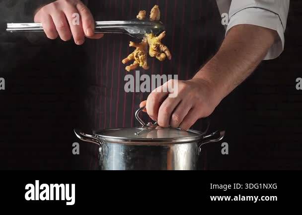 A chef holds tongs with chicken feet over a pot in the kitchen. Steam ...