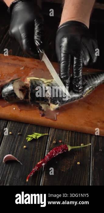 A person is cutting a whole fish on a wooden cutting board in a kitchen ...