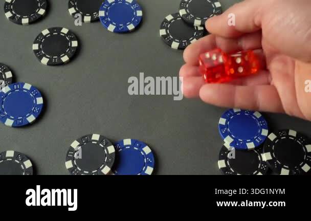 On a table covered with black and blue poker chips, one hand rolls two ...