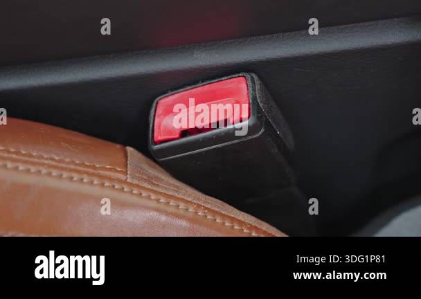 Close-up of a red car seat belt buckle next to brown leather seat ...