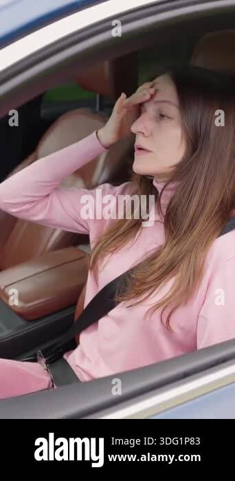 VERTICAL VIDEO: Worried woman sits in car, touching her forehead ...