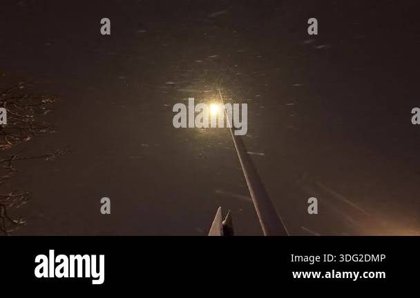 A solitary street lamp illuminates heavy snowfall at night, creating a ...