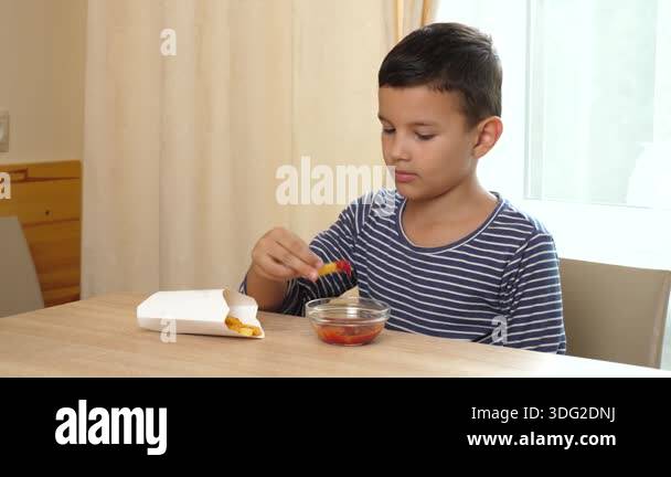 Boy eating french fries with ketchup at table during home meal Stock ...