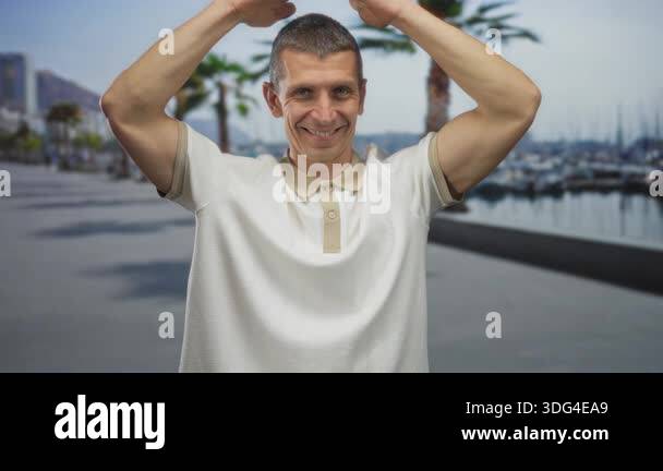 Man smiling on a seaside promenade with palm trees, making a hand ...