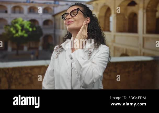 Woman wearing white jacket and glasses holds cheek for toothache inside ...