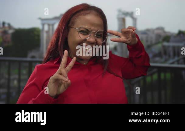 Woman in red shirt makes peace sign in front of ancient building during ...