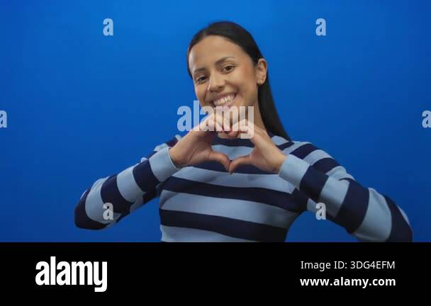 Hispanic woman smiling and forming heart shape with hands against ...