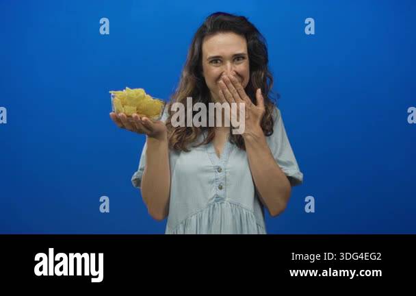 Woman holds clear bowl of potato chips while covering mouth with hand ...