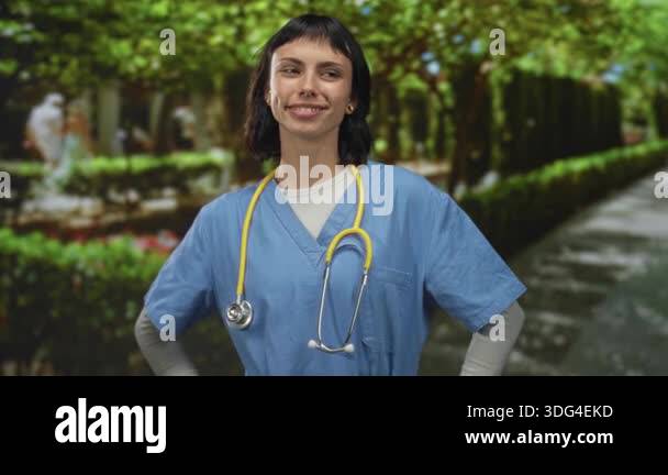 Woman doctor in blue scrubs with yellow stethoscope stands with hands ...