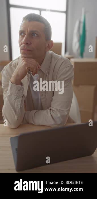 Man pondering in new apartment surrounded by moving boxes and laptop on ...