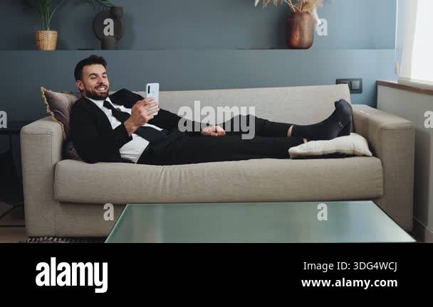 Young businessman relaxing lying on a sofa while making a video phone ...
