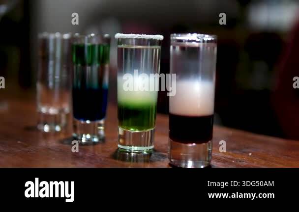 Row of colorful layered shots with bartender adding cream. High quality ...