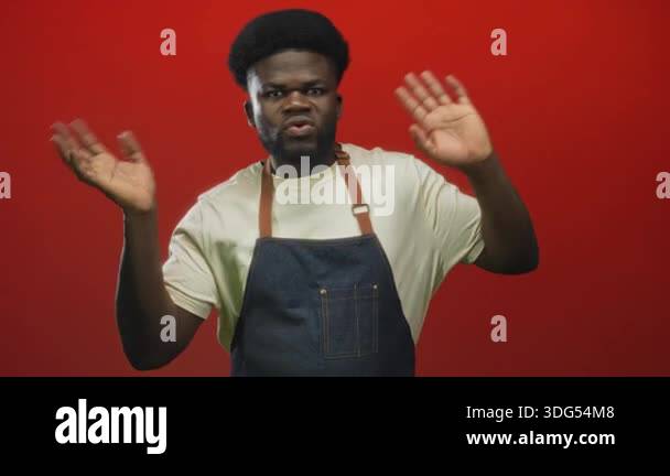 Man waving hands in studio against bright red wall wearing denim apron ...