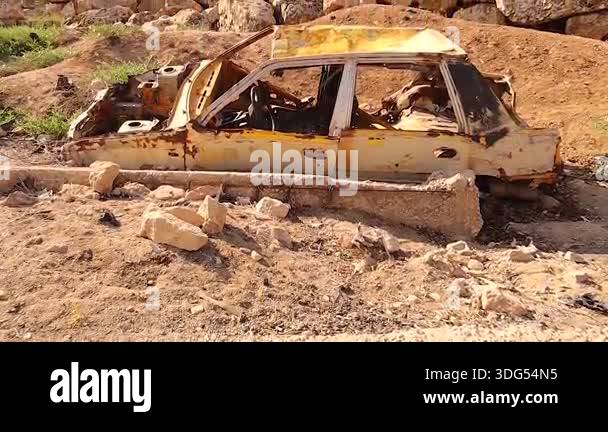 Abandoned, rusted car wreck in a desert area surrounded by rocks and ...
