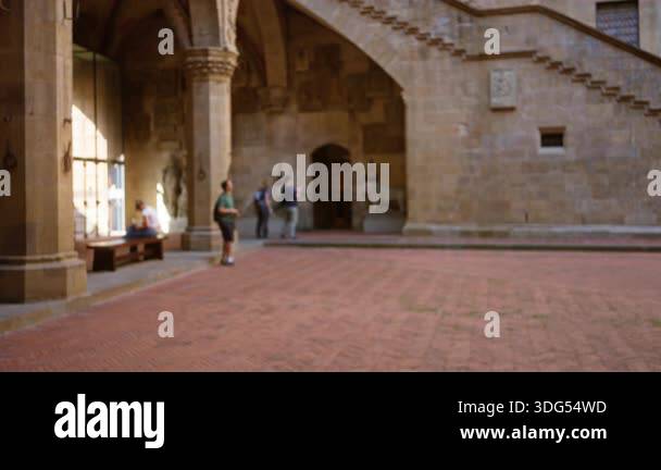 Blurred cloister courtyard with stone arches, brick paving and carved ...