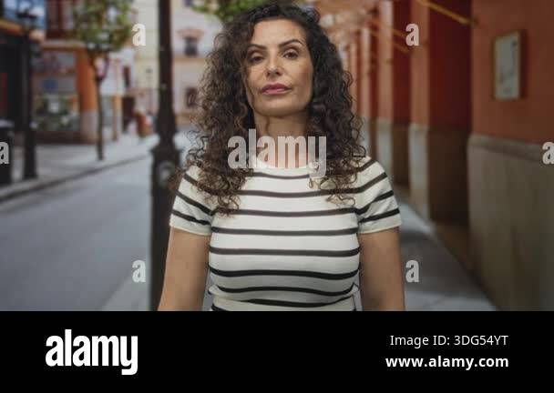 Young woman hand on forehead facing camera in front of red building on ...