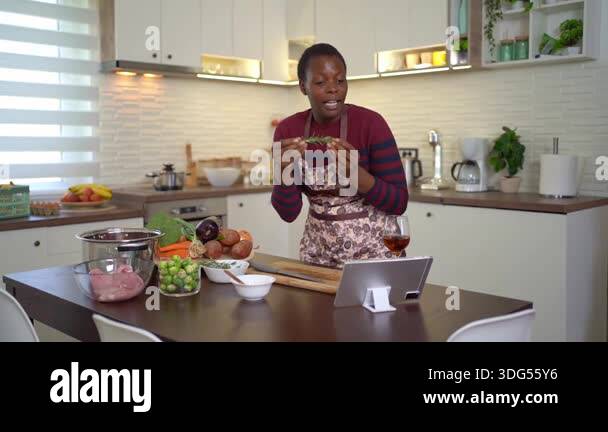 African woman following an online recipe smelling fresh rosemary while ...