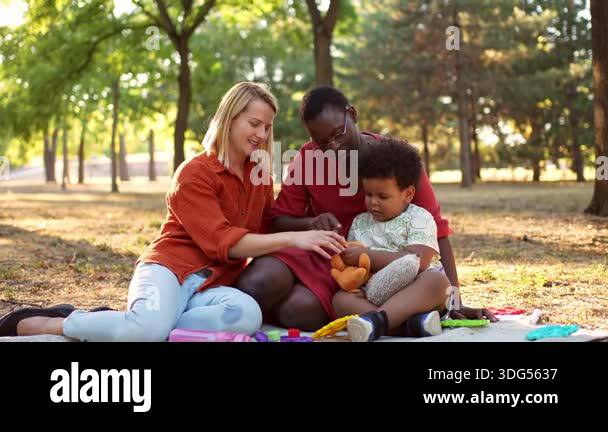 Young mixed-race family with a toddler playing with toys on a blanket ...