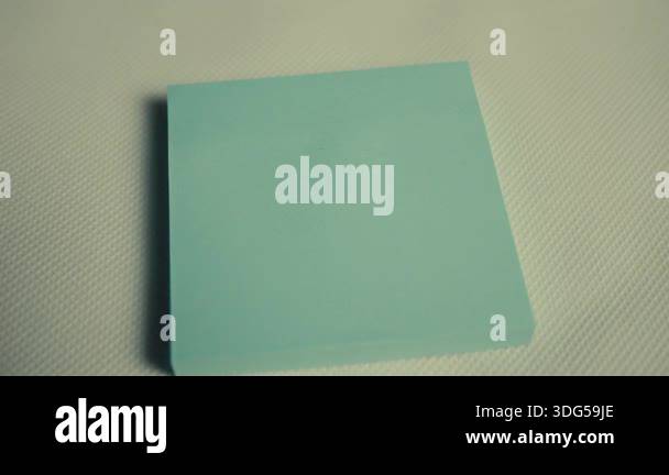 Close-up of a blank turquoise sticky note on a white textured surface ...