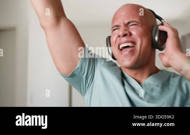 A bald man in medical scrubs enjoys a moment of pure joy, singing and ...