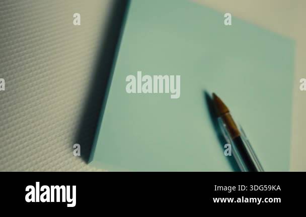 Close-up of a blue sticky note with a ballpoint pen on a white textured ...