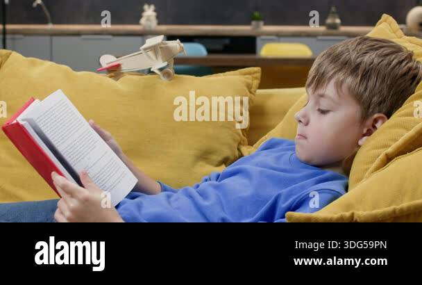 Little boy reads book and looks at wooden airplane put on comfortable ...