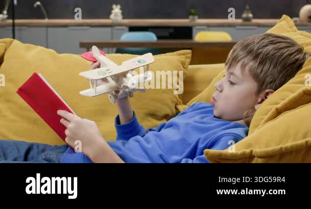 Little boy reads book and plays with plywood toy airplane on sofa with ...