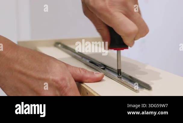 Man fixes sliding rail onto drawer side using screwdriver during ...