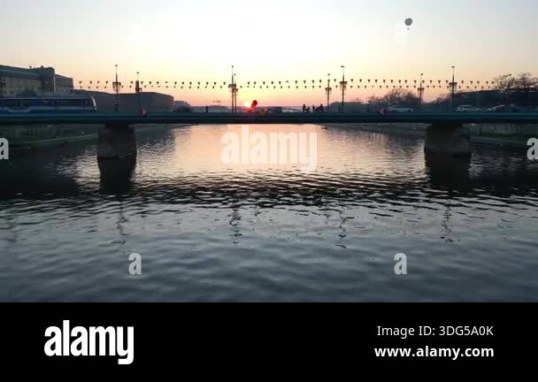 Aerial view of tram crossing a bridge over a river at sunset with cars ...