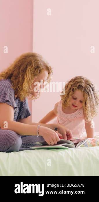 Caucasian mother and her cute curly haired daughter reading a book ...