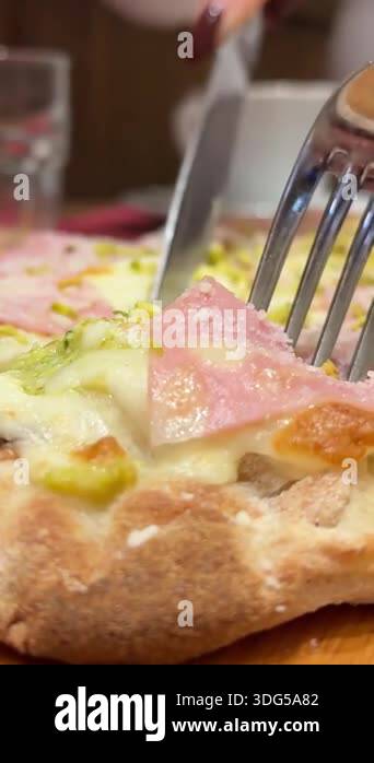 Close up of a man cutting hot cheese pizza with a fork and knife in an ...