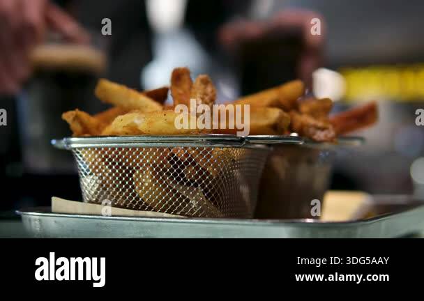 Warm lighting highlights hand reaching for fries in metal basket ...