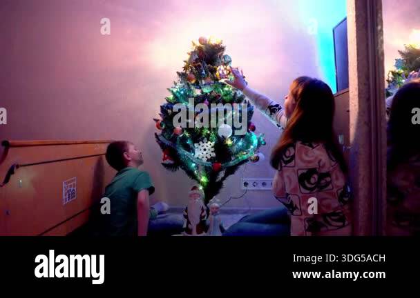 A first-grade boy and his mother decorate an artificial Christmas tree ...