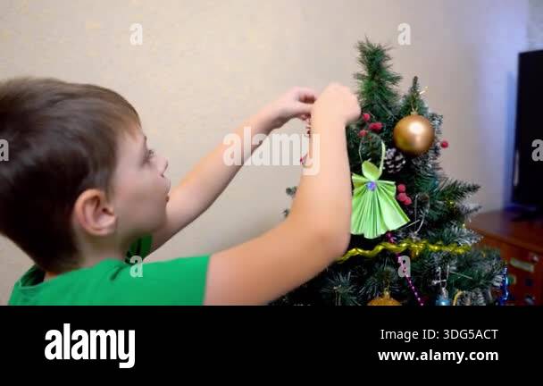 A first-grader boy decorates an artificial Christmas tree at home. A ...