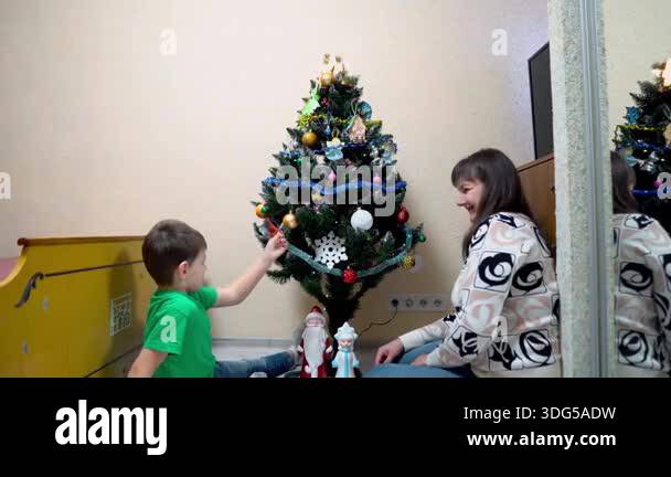 A first-grade boy and his mother decorate an artificial Christmas tree ...