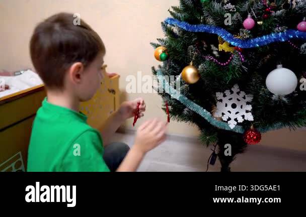 A first-grader boy decorates an artificial Christmas tree at home. A ...