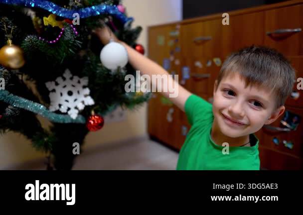 A first-grader boy decorates an artificial Christmas tree at home. A ...