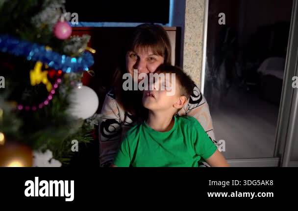 A first-grade boy and his mother decorate an artificial Christmas tree ...