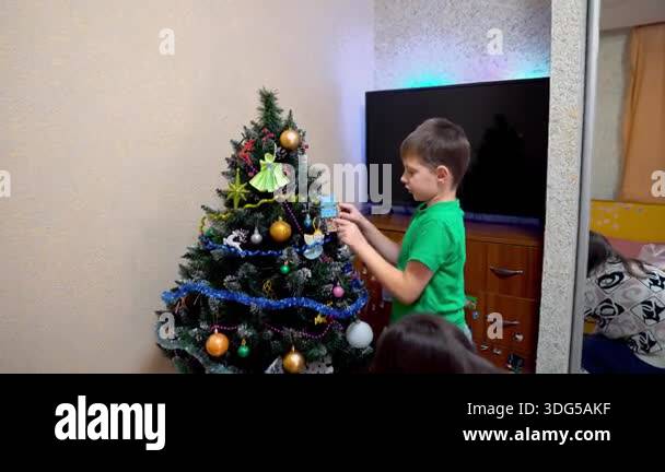 A first-grade boy and his mother decorate an artificial Christmas tree ...