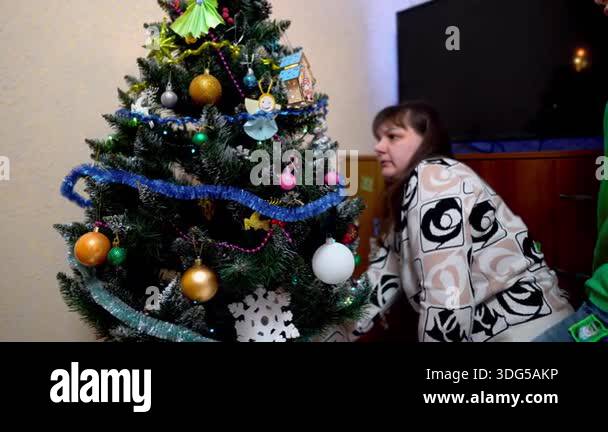 A first-grade boy and his mother decorate an artificial Christmas tree ...