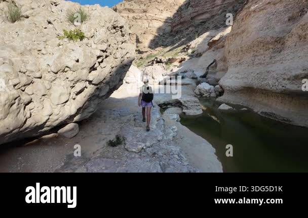 Woman backpacking, hiking through a rocky dry wadi in Wadi Hadhbram ...