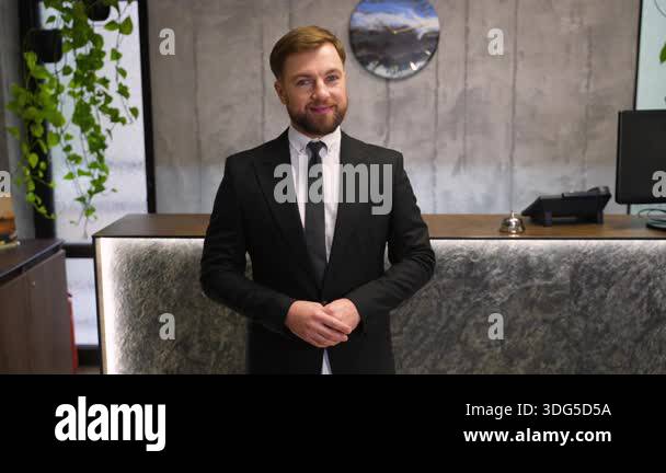 Friendly hotel manager standing at the reception desk, smiling and ...