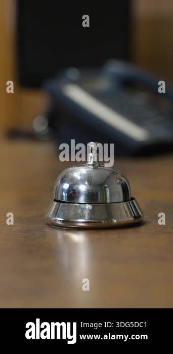 Female guests hand ringing a silver service bell on a wooden reception ...