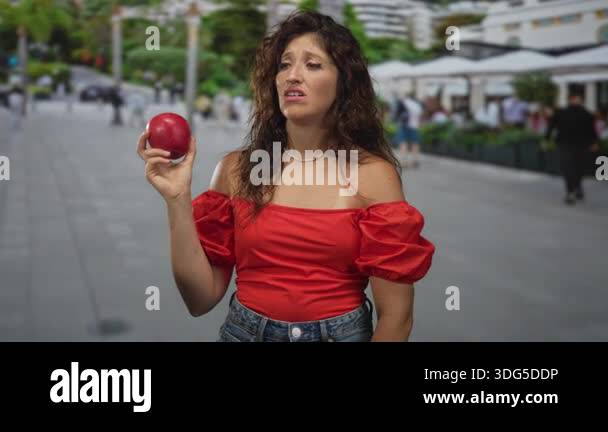 Young woman holds red apple and covers face with hand while wearing red ...